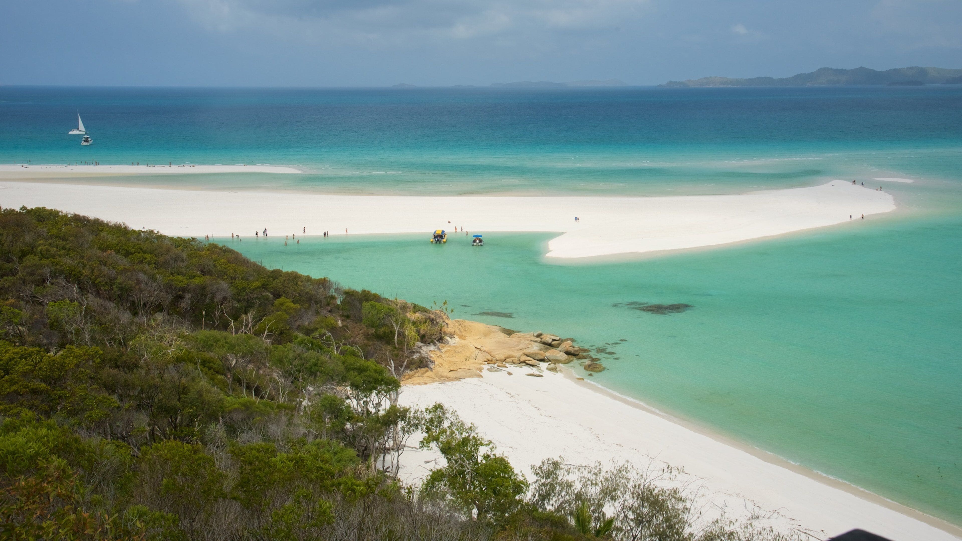 Uma praia com águas turquesa cristalinas, areia branca e um pequeno barco ao longe.