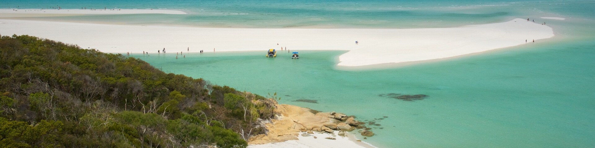 Uma praia com águas turquesa cristalinas, areia branca e um pequeno barco ao longe.