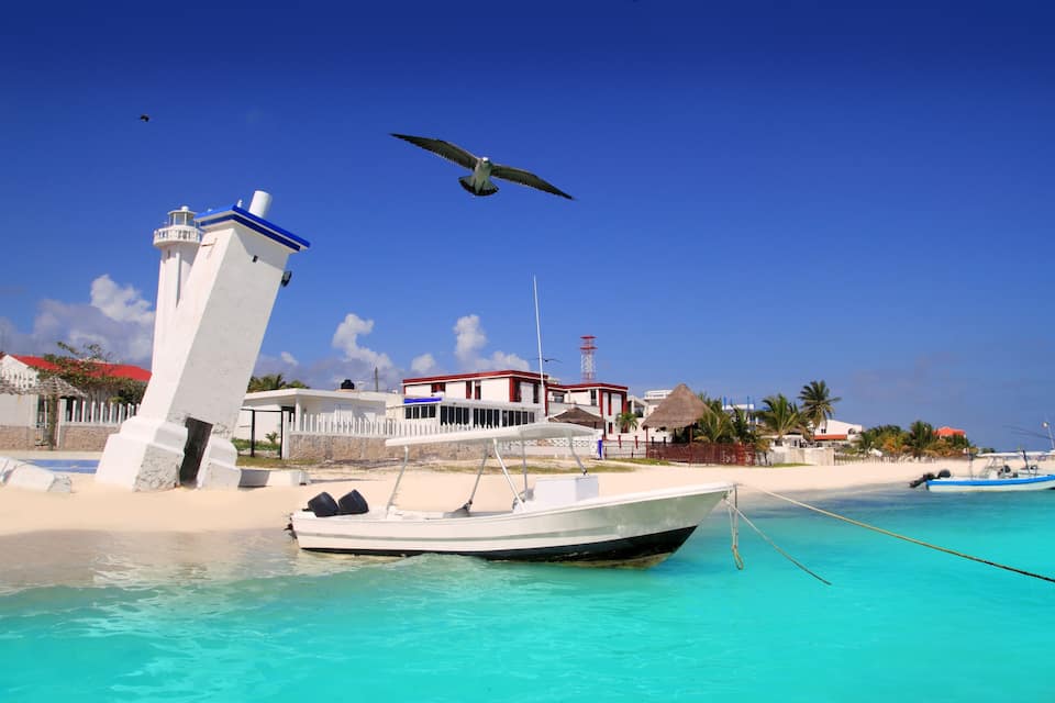Uma praia com um farol branco, um barco e uma gaivota voando.