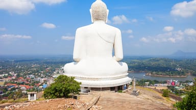 Uma grande estátua branca de uma figura sentada com parte superior arredondada, rodeada por uma base circular, com vista para uma cidade e rio.