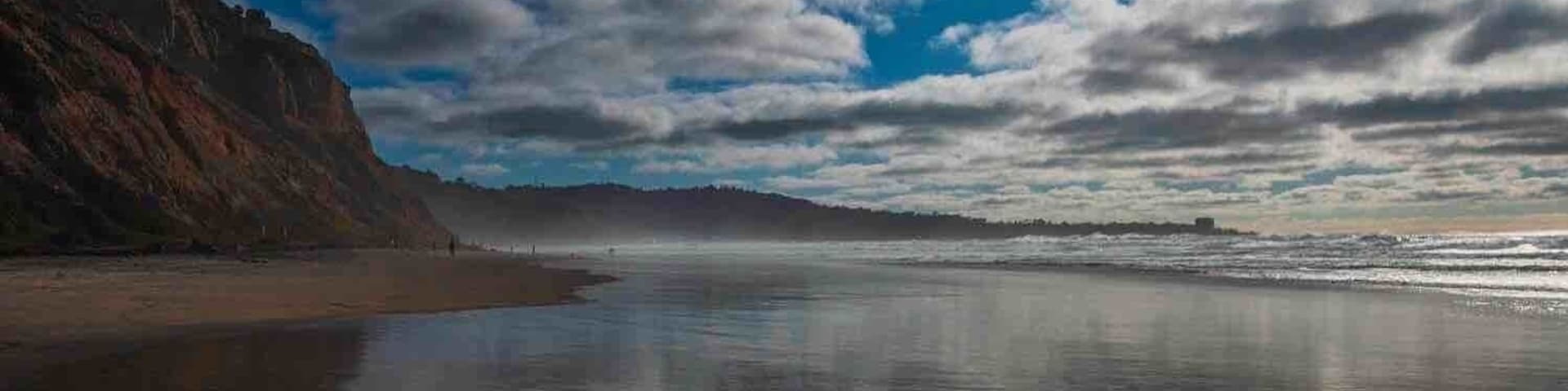 Uma praia com um penhasco rochoso à esquerda e um mar calmo.