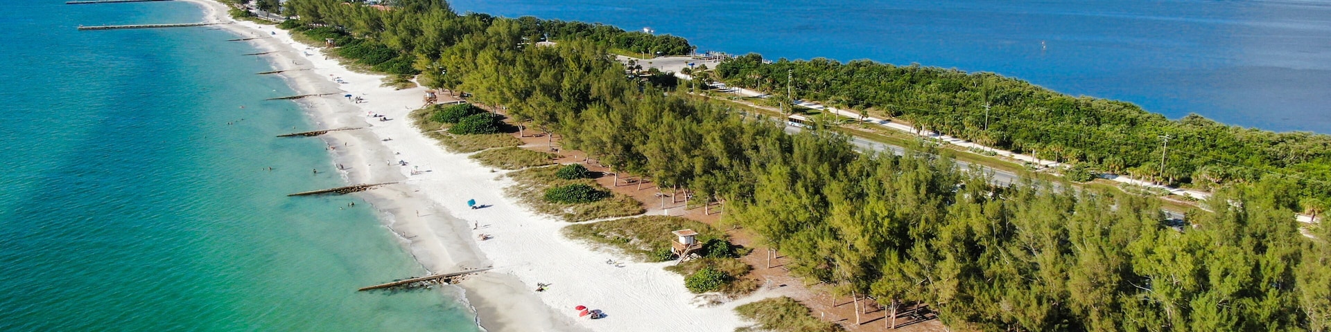 Uma praia costeira com águas turquesa cristalinas, areal arenoso e uma área florestal densa.