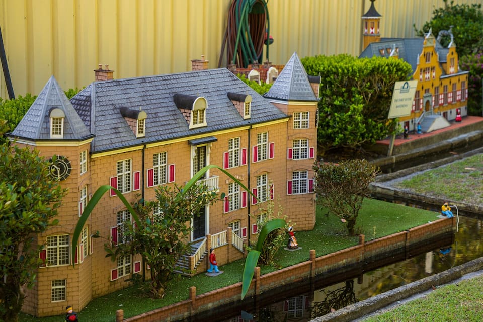 Maquete de um edifício histórico com persianas vermelhas e um canal em frente.