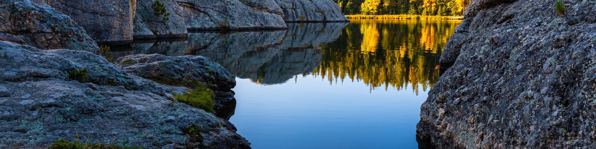 Um lago tranquilo rodeado por terreno rochoso e floresta densa.