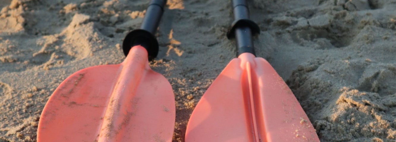 Duas pranchas de remo laranja numa praia de areia, com um poste preto entre elas.
