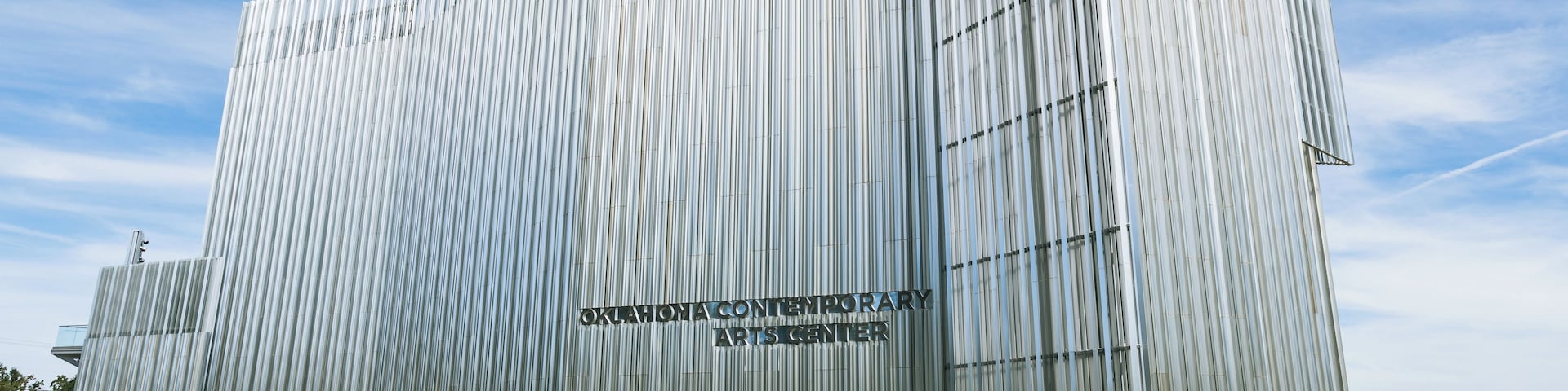 Um edifício moderno com linhas verticais, com a placa 'OKLAHOMA CONTEMPORARY ARTS CENTER'.
