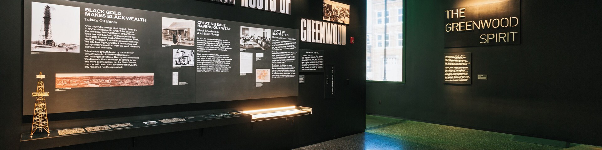 Uma exposição com painéis informativos intitulados 'The Roots of Greenwood' e 'The Greenwood Spirit'.