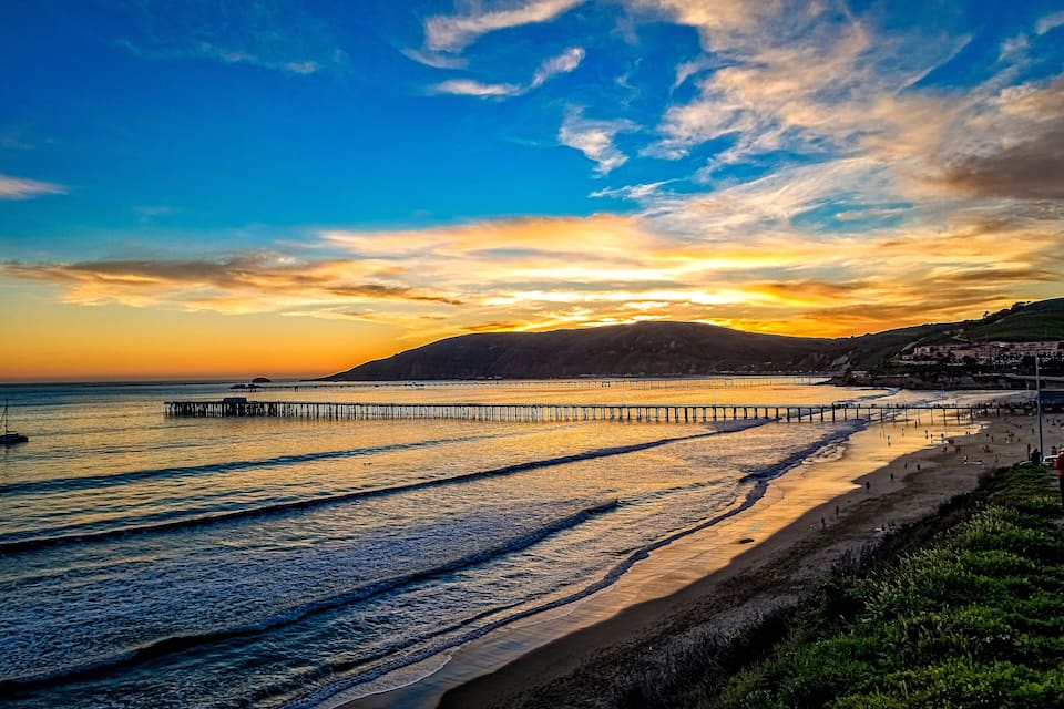 Um pôr do sol sobre uma praia com um cais que se estende para a água.