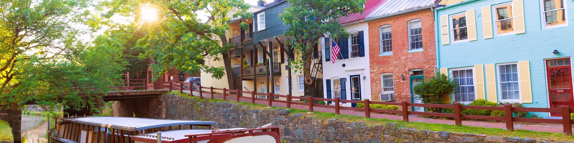 Um canal estreito com um barco a remos atracado à esquerda, ladeado por edifícios históricos coloridos e uma parede de pedra.