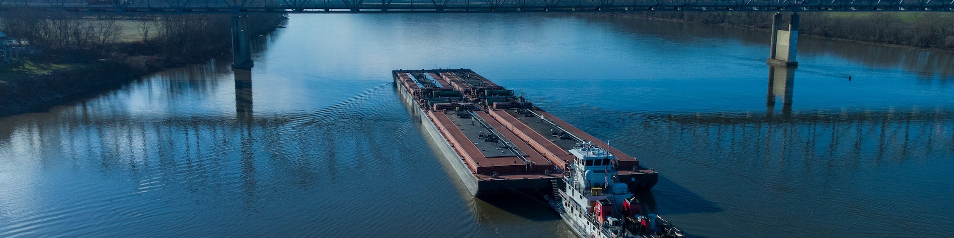 Um navio de carga em um rio calmo, com uma ponte ao fundo.