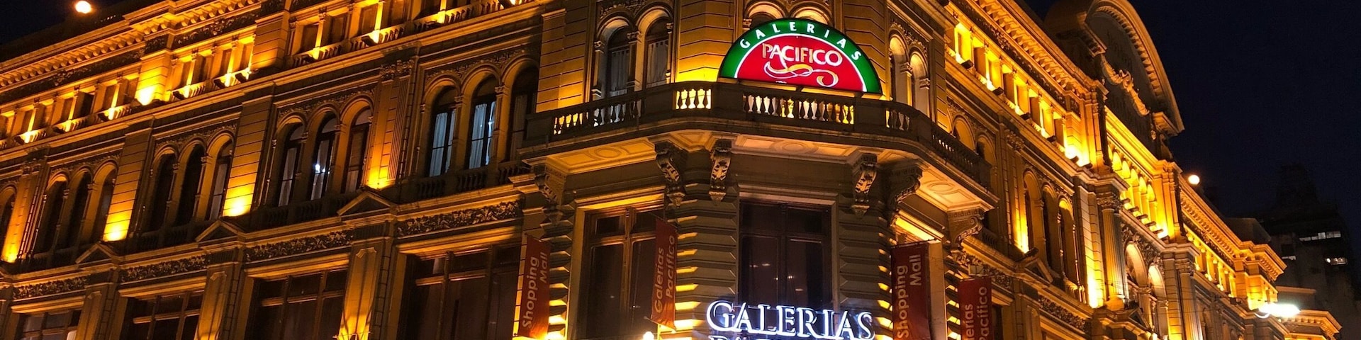 Um edifício histórico bem iluminado com arquitetura ornamentada e um letreiro chamativo 'Galerias Pacifico'.