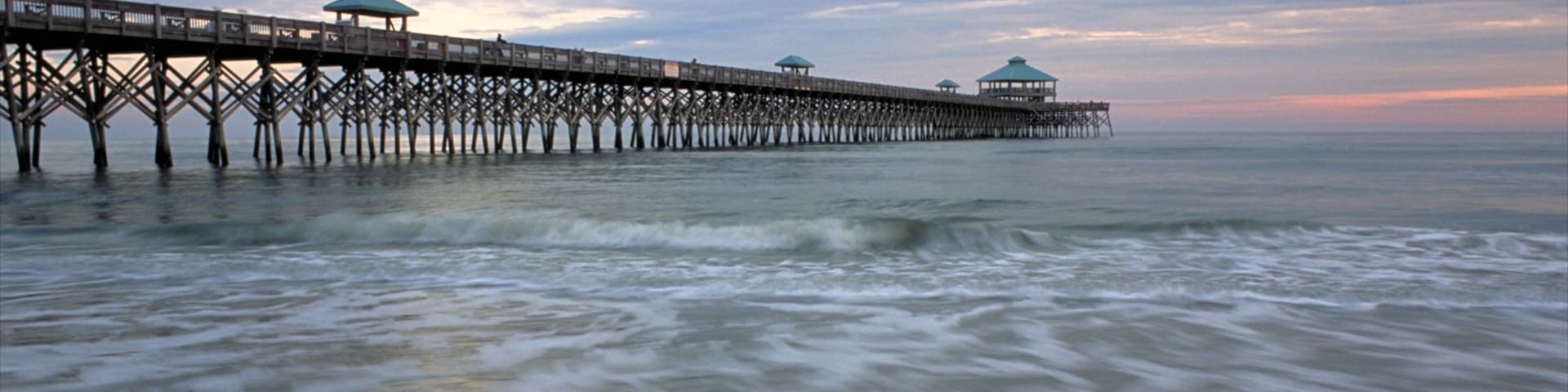 Folly Beach que inclui um pôr do sol, uma ponte e uma praia