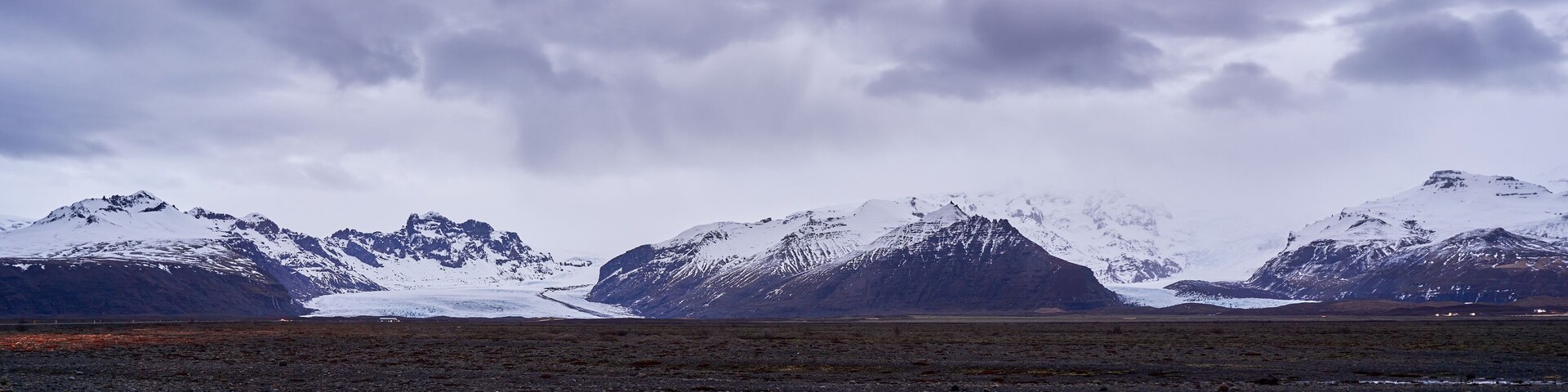 Um glaciar com montanhas cobertas de neve ao fundo.