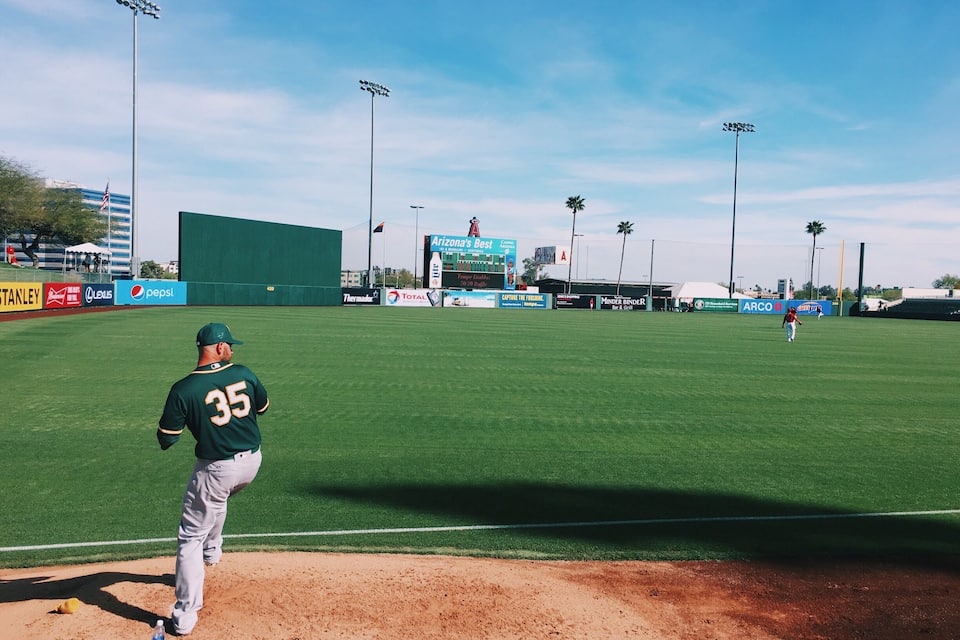 Um campo de beisebol com anúncios, um jogador de uniforme verde e céu claro.