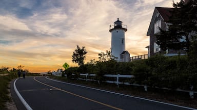 Uma estrada serpenteia por um farol branco e uma casa com telhado vermelho.