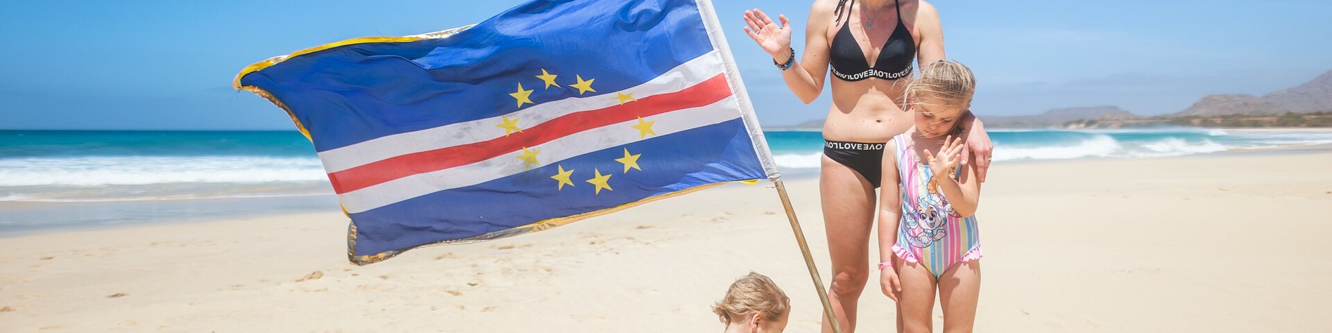 Uma praia com uma bandeira, uma mulher e uma criança.