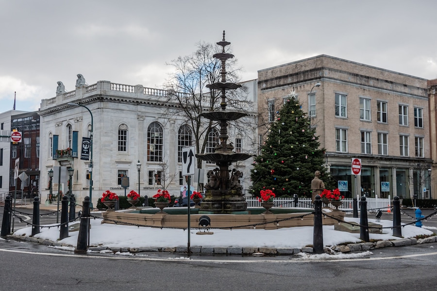 Uma praça pública com uma fonte, uma árvore de Natal e edifícios históricos.