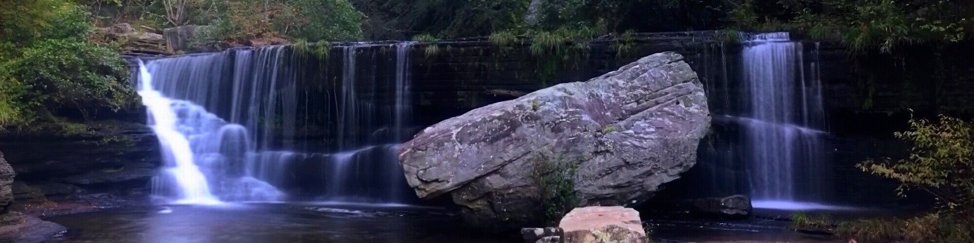 Uma cascata com várias quedas d'água, cercada por floresta densa e árvores com cores de outono.