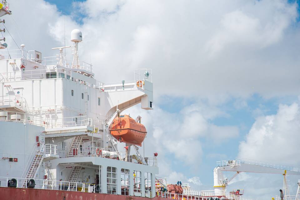 Um grande navio branco com um bote salva-vidas e uma grua.