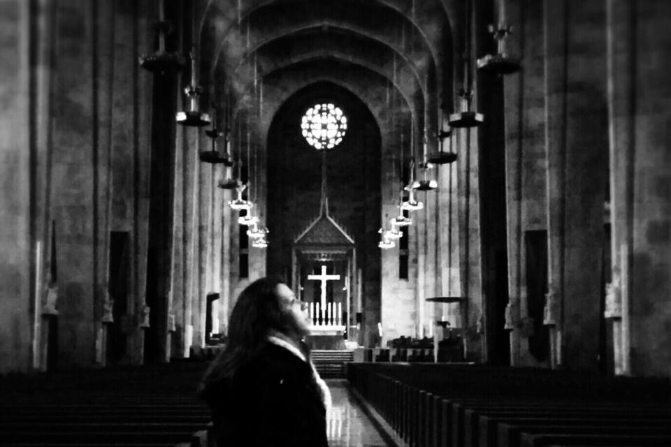 Uma pessoa está em uma nave de igreja, com uma cruz ao fundo.