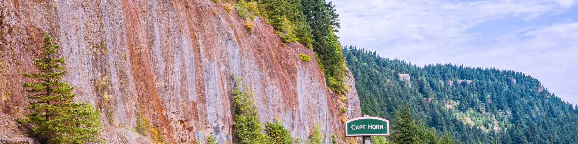 Uma estrada serpenteando ao longo de um penhasco íngreme e rochoso, com uma placa indicando 'Cape Horn'.