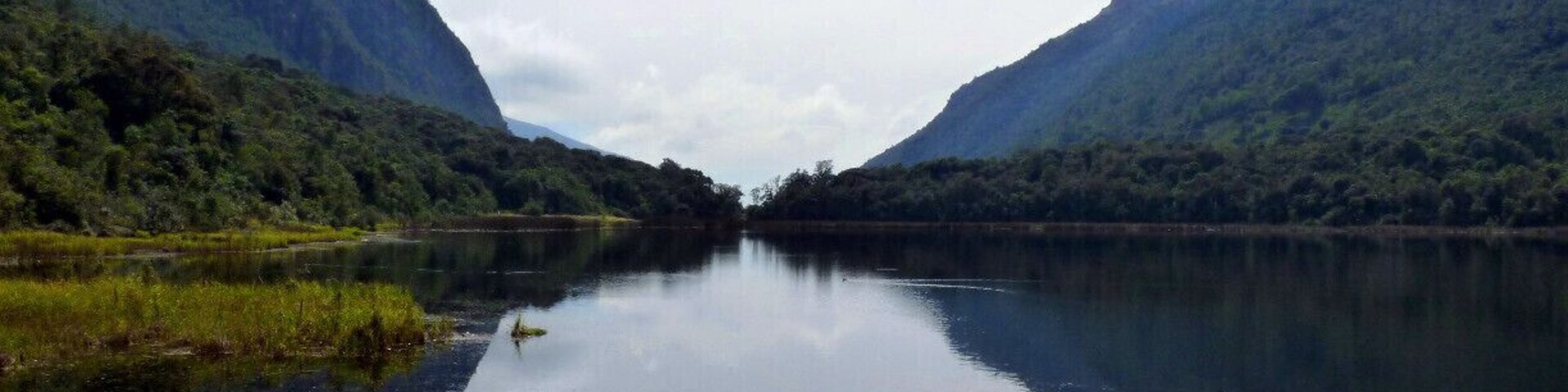 Um rio tranquilo ladeado por montanhas verdes e exuberantes sob um céu nublado.