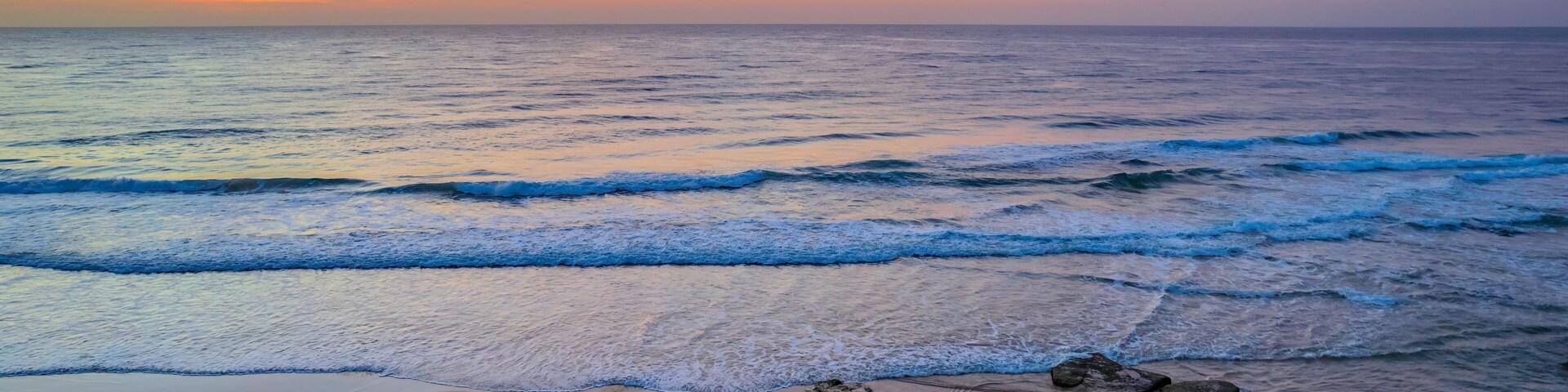 Uma praia com ondas e um céu ao pôr do sol.
