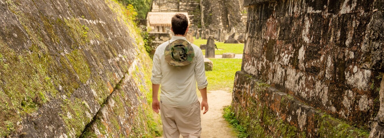 Um homem caminhando por uma trilha de terra entre antigas construções de pedra.