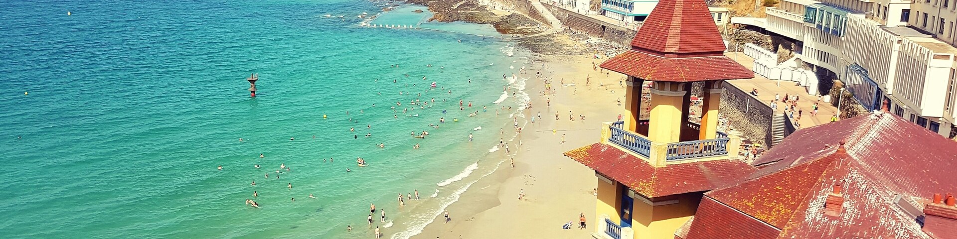 Uma vila costeira com praia, farol e edifícios residenciais.