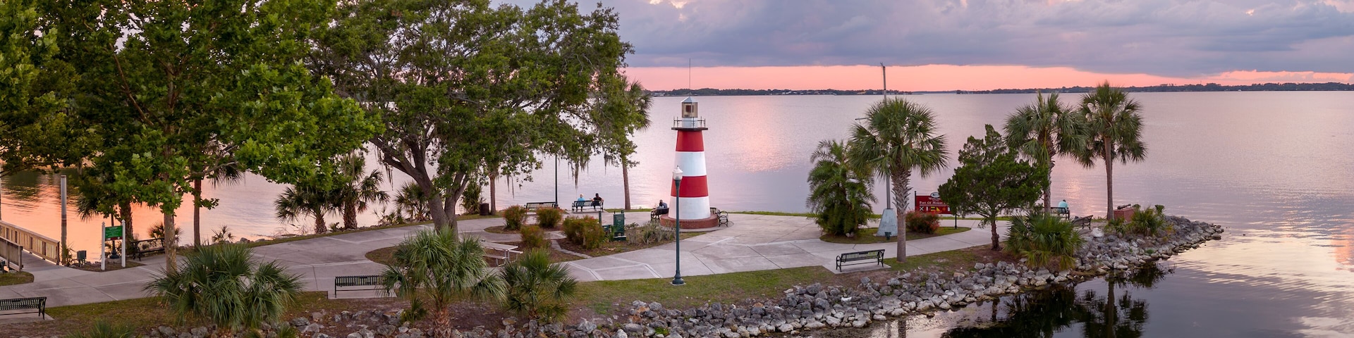 Um farol, palmeiras, um lago calmo e um céu ao pôr do sol.