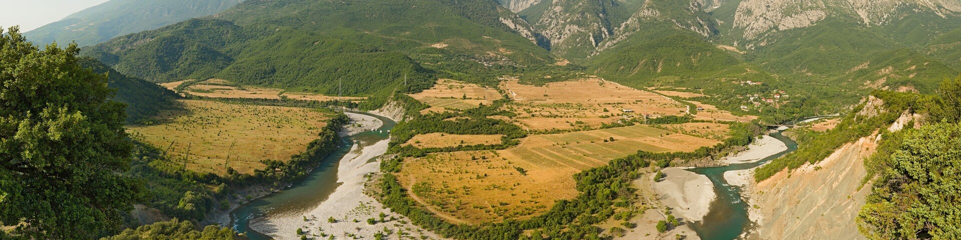 Paisagem montanhosa com um rio serpenteando por um vale, cercado por vegetação exuberante e terreno rochoso.