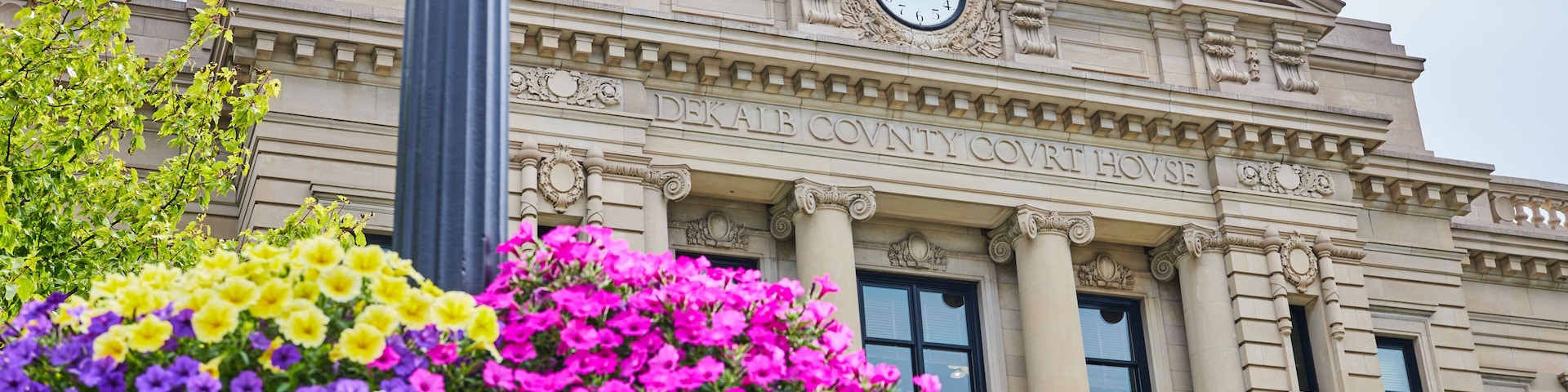 Um edifício com colunas e um relógio, com a inscrição 'DEKAIB COUNTY COURT HOUSE'.