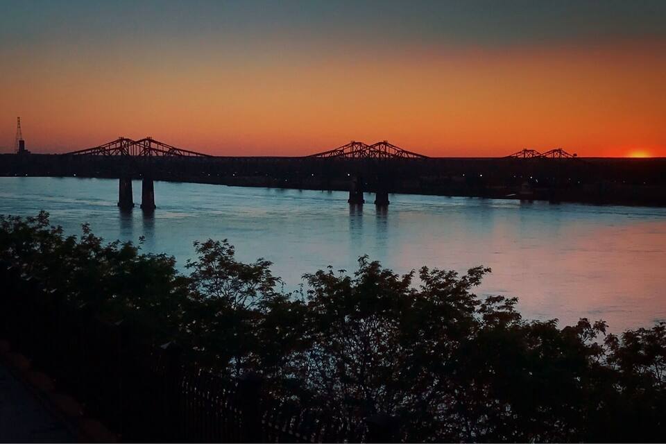 Um pôr do sol sobre uma ponte, com águas calmas abaixo.