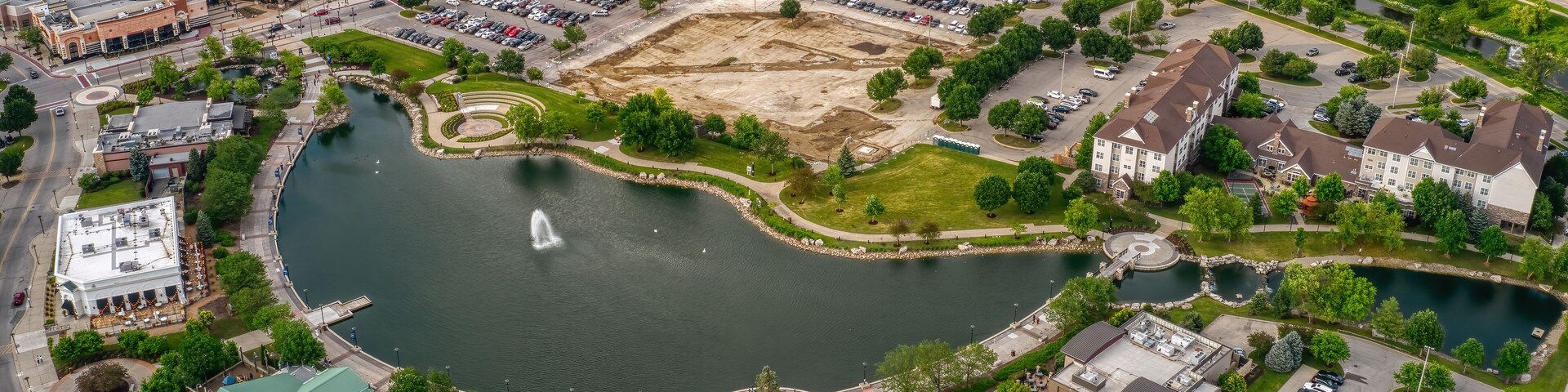 Vista aérea de uma cidade com um lago grande, edifícios ao redor e um estacionamento.