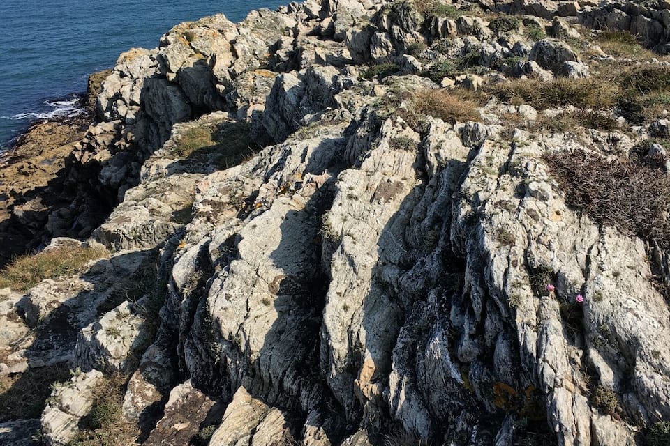 Um litoral rochoso com terreno acidentado e vegetação escassa.