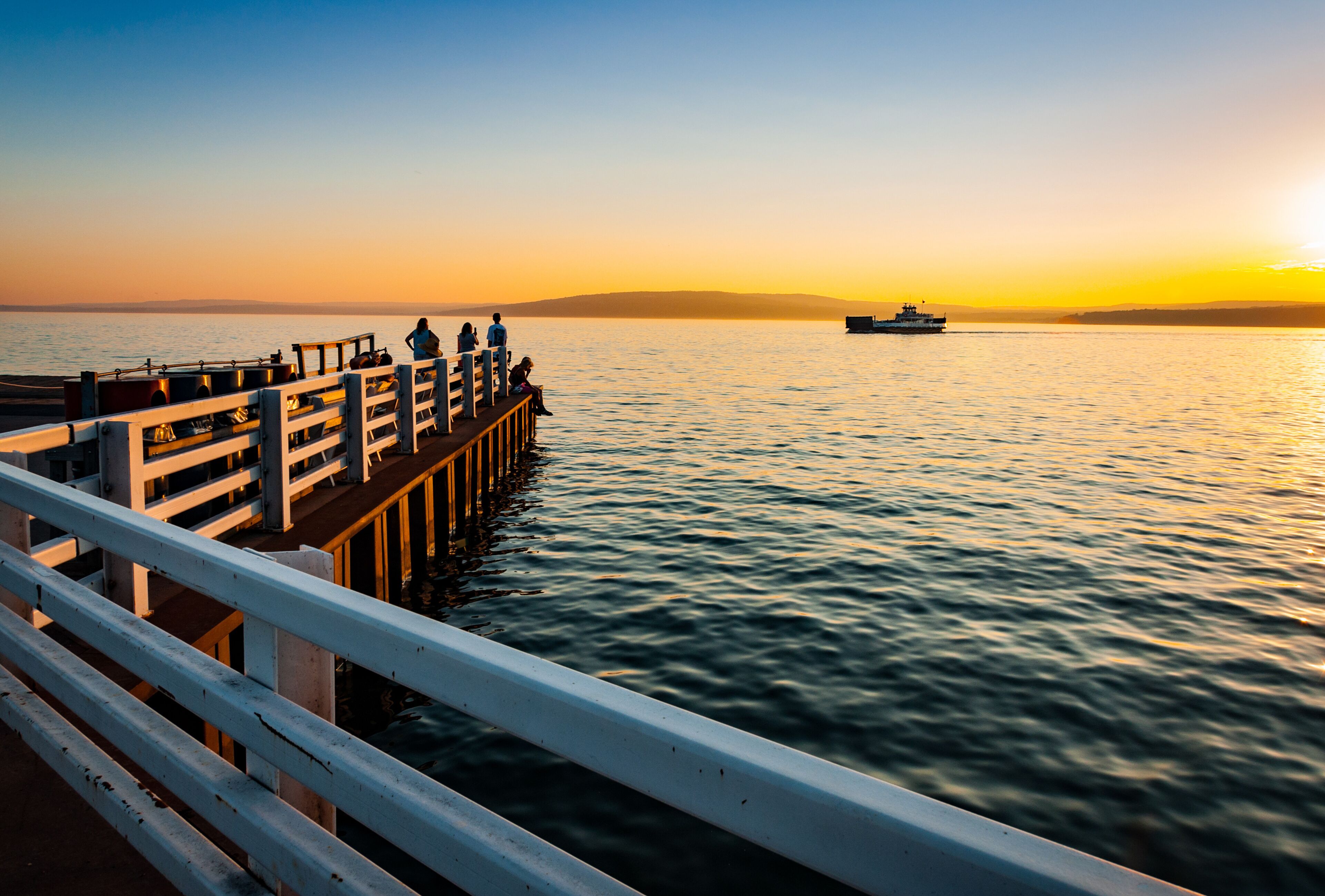 Um cais se estendendo sobre águas calmas ao pôr do sol, com um barco ao longe.