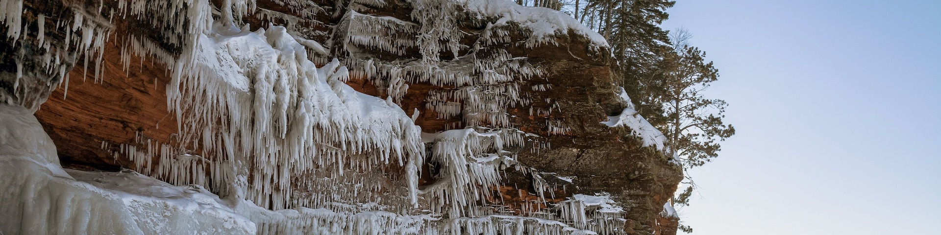 Um penhasco congelado com iciclos e árvores cobertas de neve.