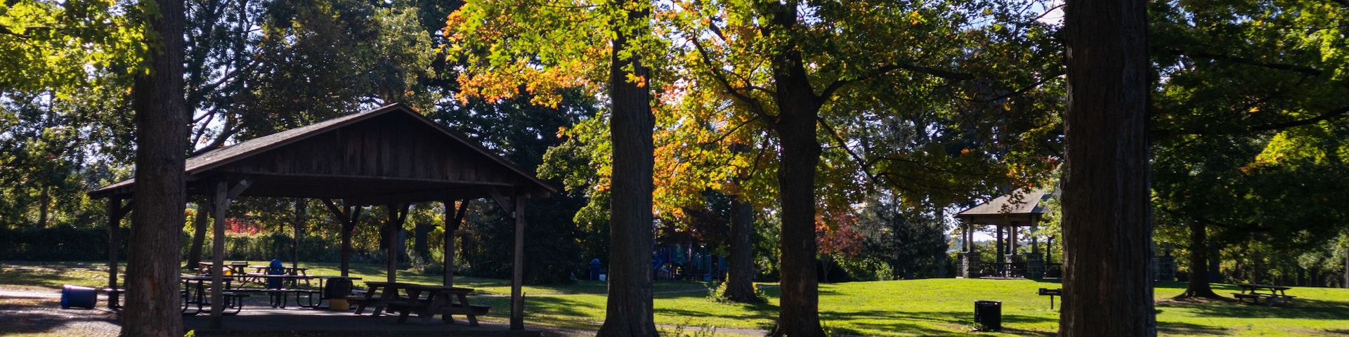 Um parque com mesas para piquenique, um coreto e árvores altas com folhagem de outono.