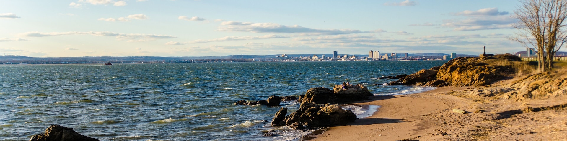 Uma praia com rochas e um horizonte urbano distante.