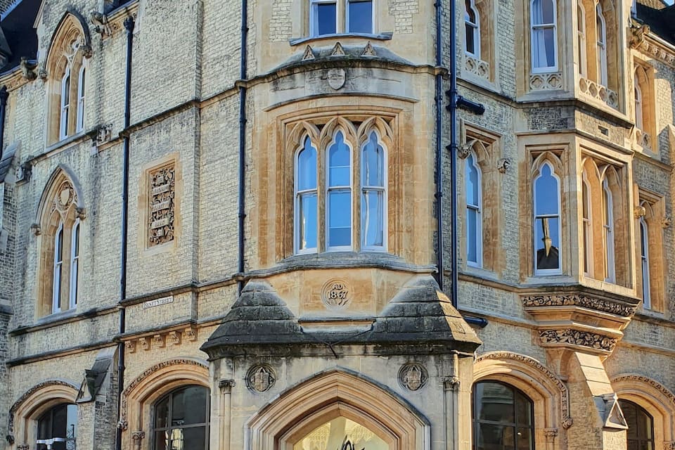 Um edifício histórico de pedra com janelas em arco e um emblema circular proeminente na entrada.