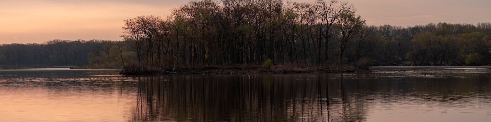 Um lago calmo com uma ilha arborizada no centro.