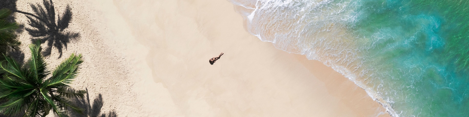 Uma praia de areia com águas turquesa cristalinas e palmeiras.