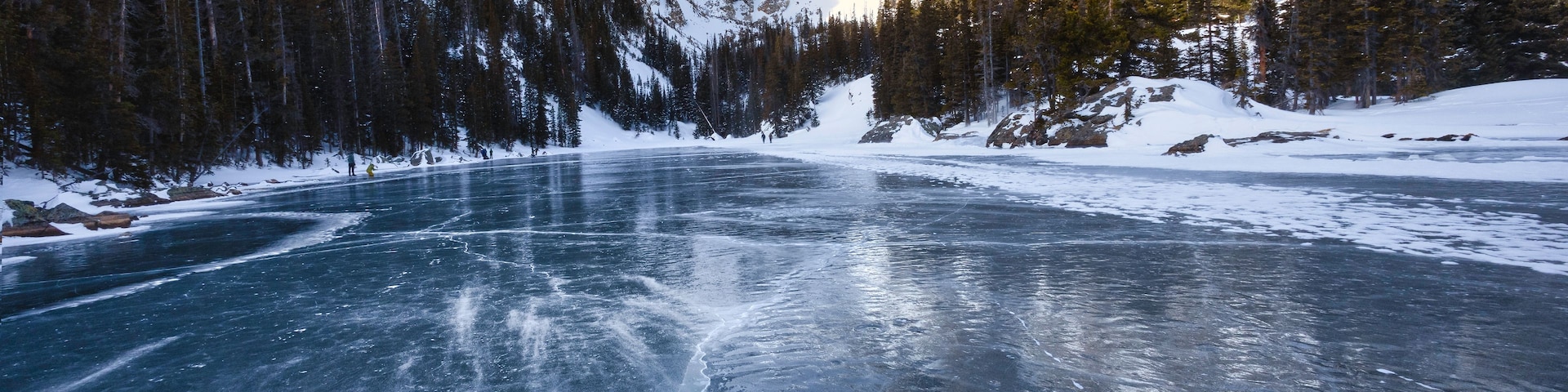 Um lago congelado rodeado por montanhas cobertas de neve e florestas densas.