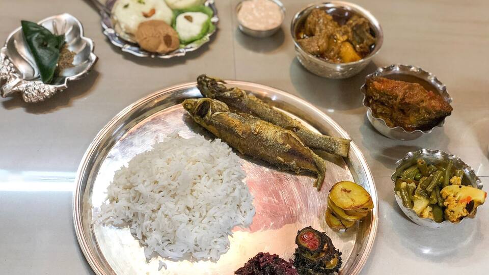 Uma refeição tradicional indiana com arroz, peixe e diversos acompanhamentos em um prato de prata.
