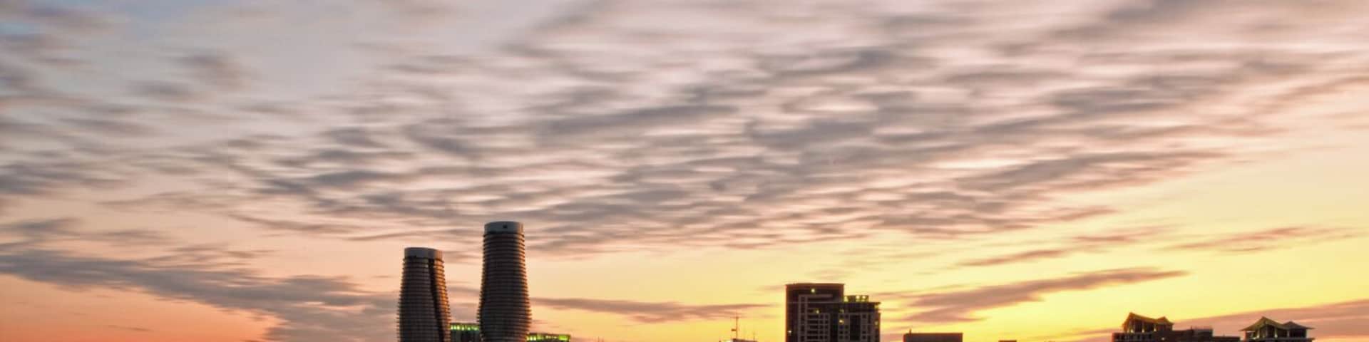 Horizonte urbano ao entardecer com edifícios iluminados e céu em tons de pôr do sol.