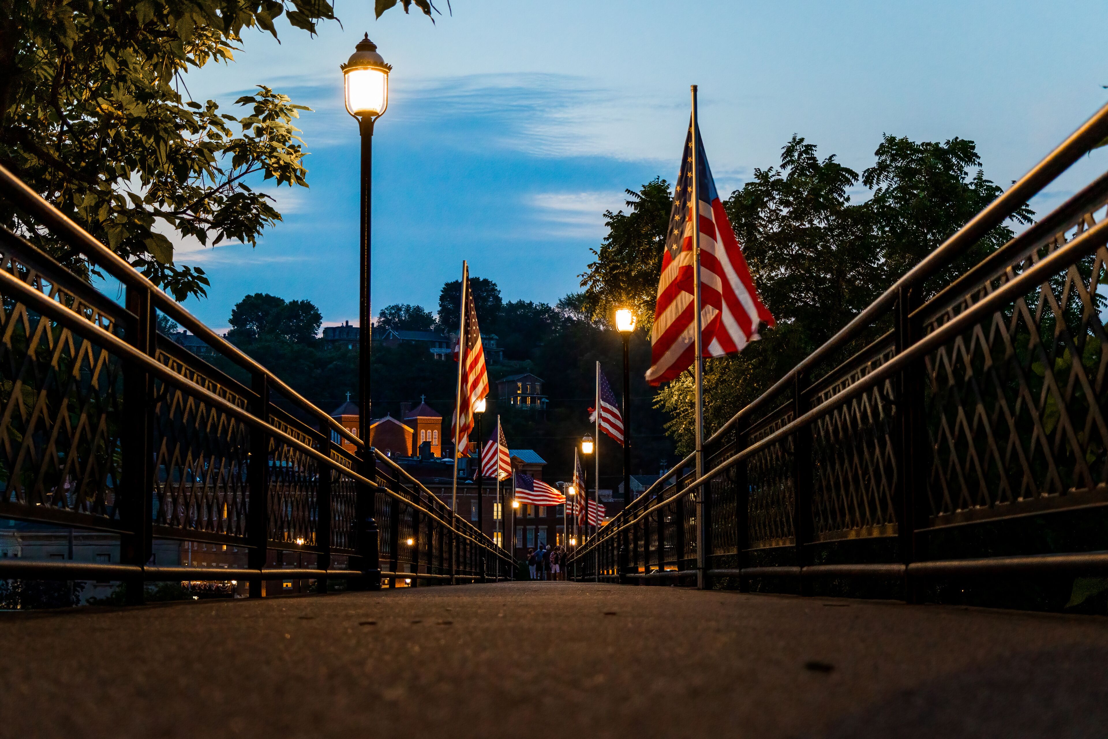 Uma ponte com bandeiras americanas, um poste de iluminação e edifícios ao fundo.
