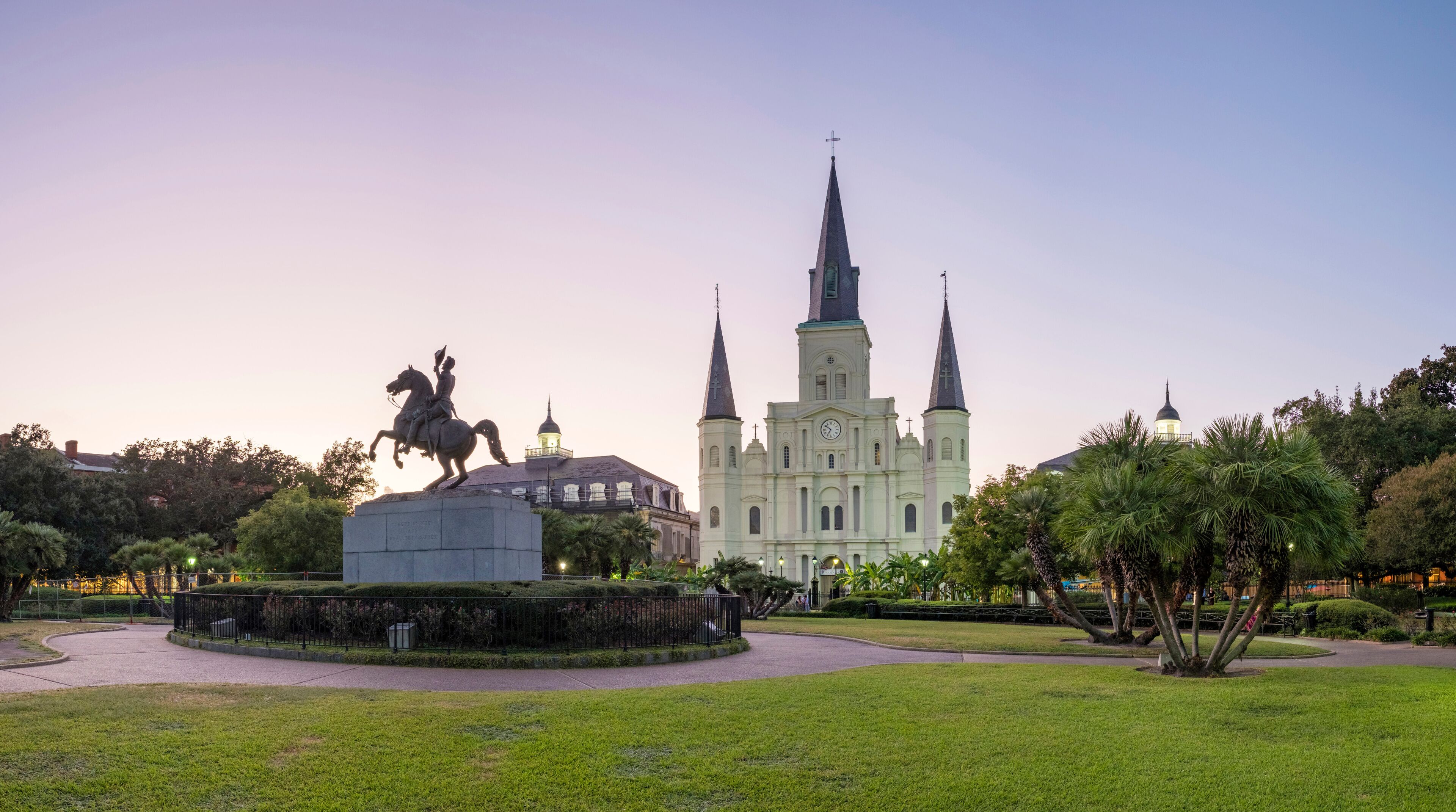 Uma estátua de uma figura a cavalo em um parque, com uma igreja de três torres ao fundo.