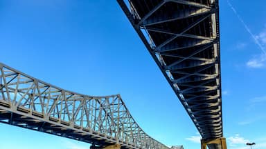 Uma grande ponte de aço com design curvo, sustentada por várias pilastras, sob um céu azul claro.