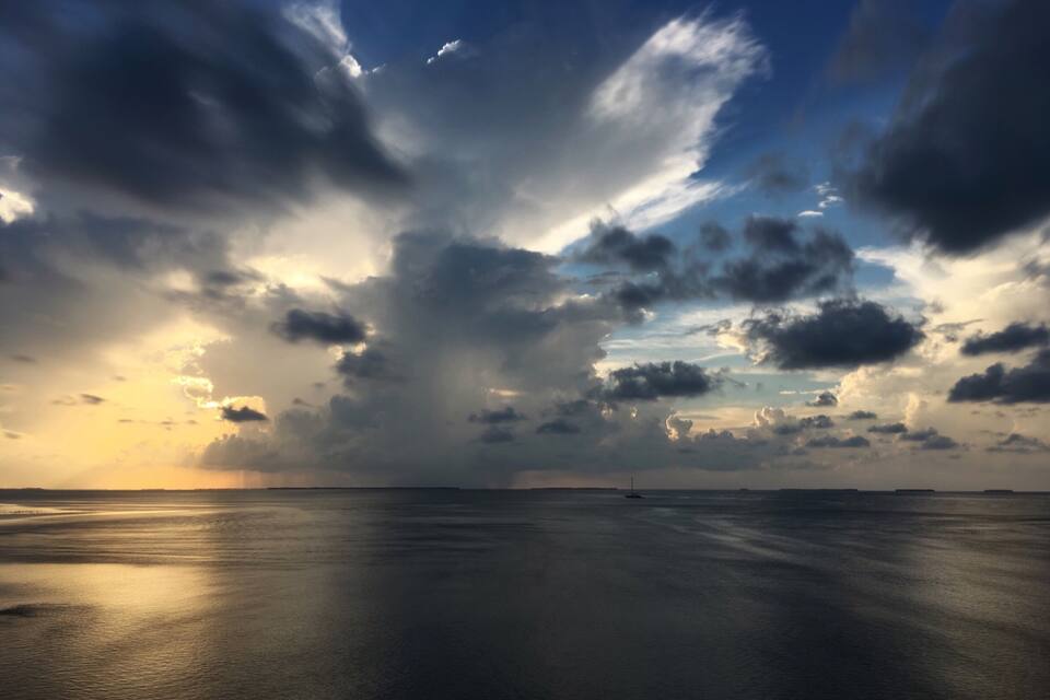 Um vasto oceano com um barco ao longe, sob um céu dramático com nuvens dispersas.