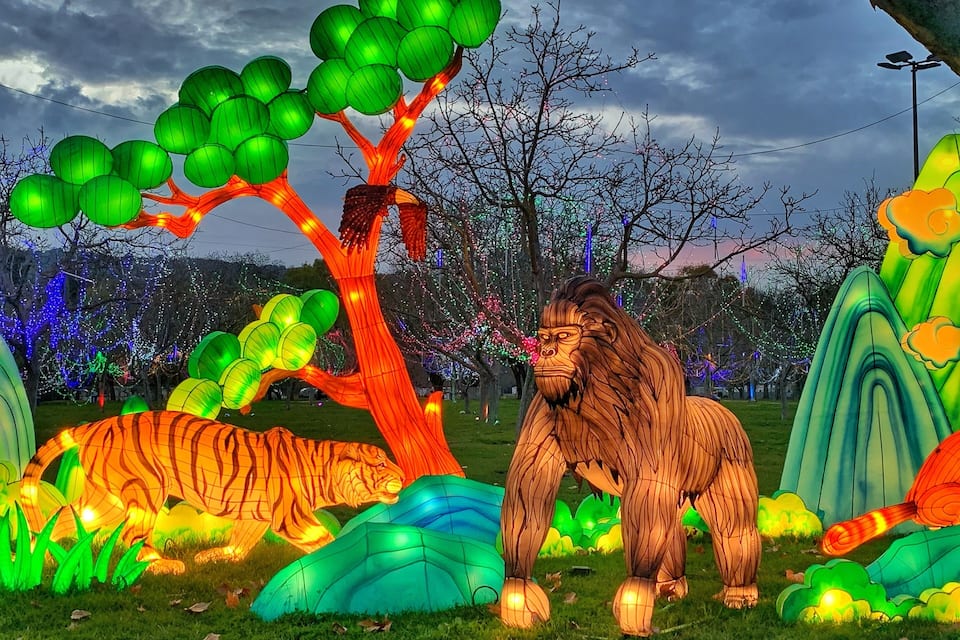 Uma grande árvore iluminada com lanternas verdes, um tigre e um gorila.